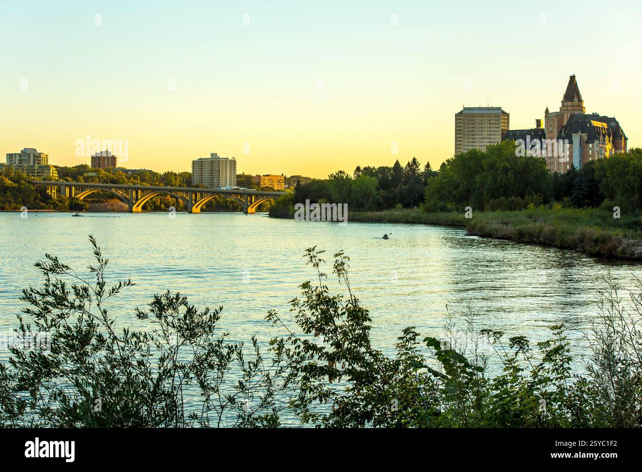 Bridge spans a river with a city in the background. Trees line the ...