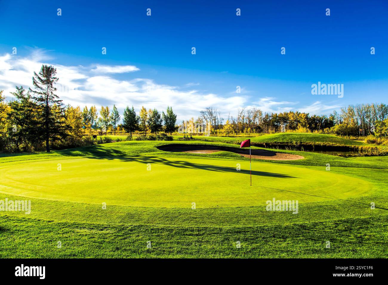 Golf course with a green grassy area and a red flag. The flag is on the ...