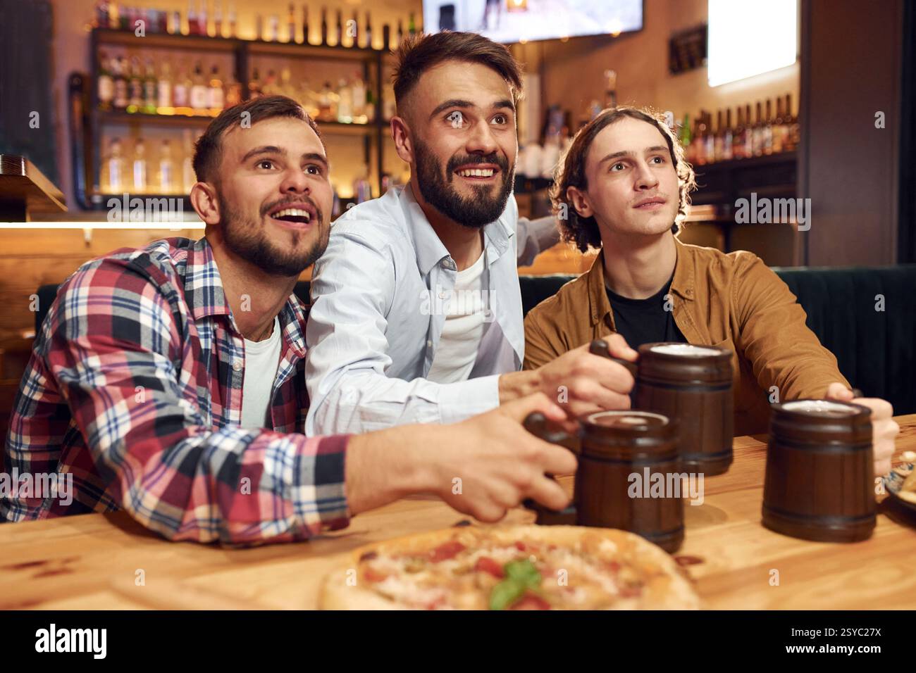 Front view. Soccer fans. Three friends are in the bar drinking beer and ...