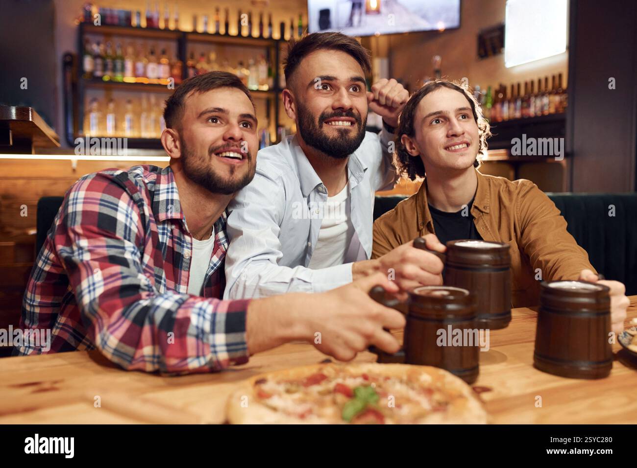 Front view. Soccer fans. Three friends are in the bar drinking beer and ...