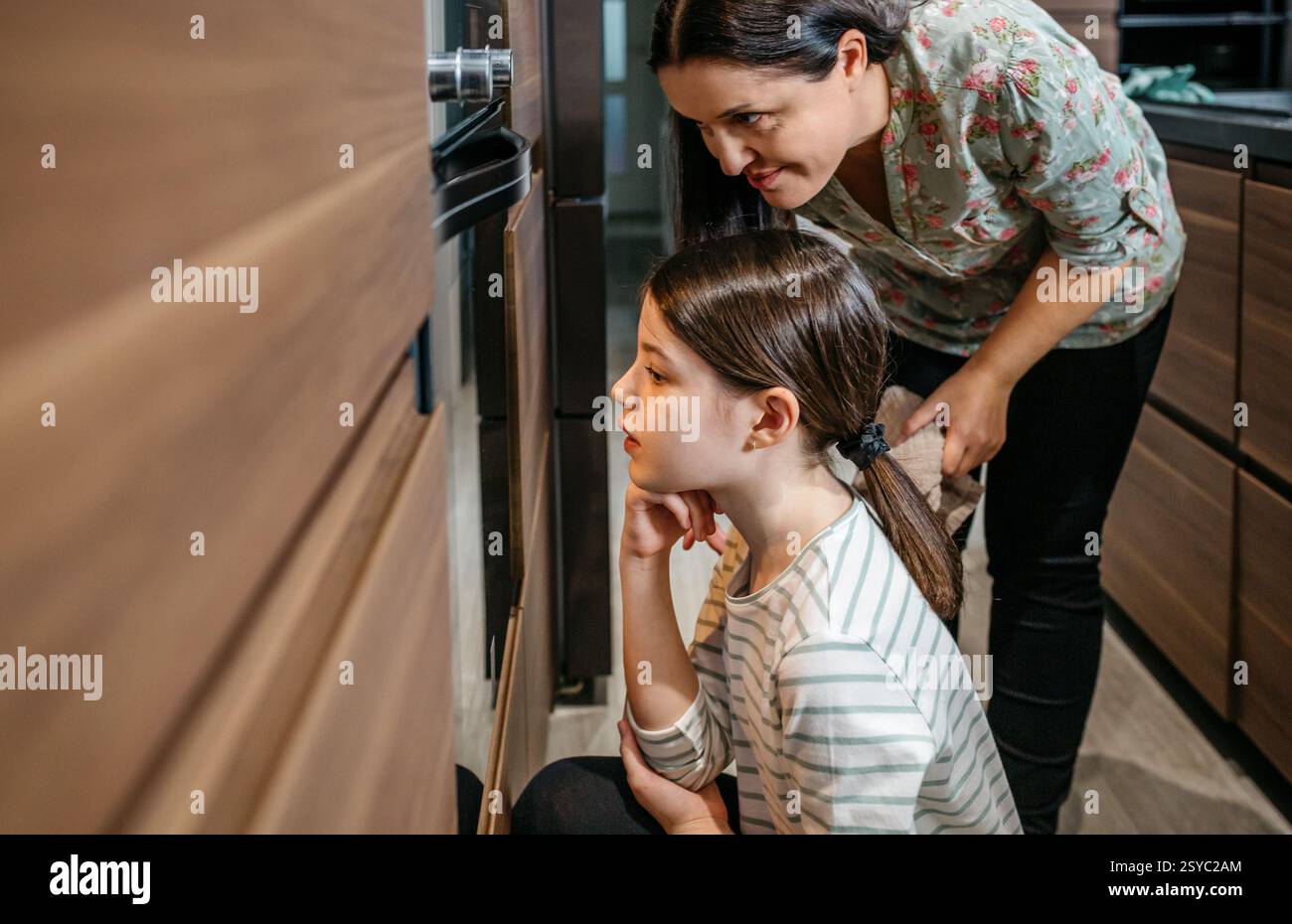 Mother and daughter watching baking in oven in kitchen. Family time ...