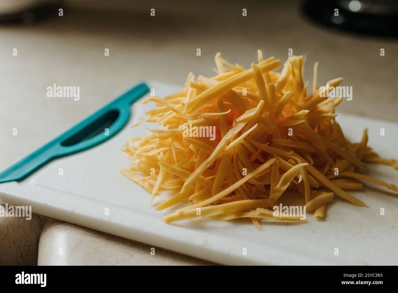 Freshly grated pile of cheddar cheese sits on cutting board Stock Photo ...
