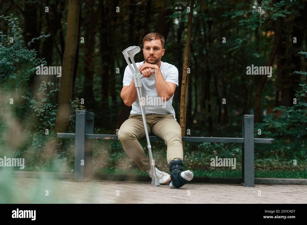 Sitting, feeling bored and sad. Man with crutches is in the park ...