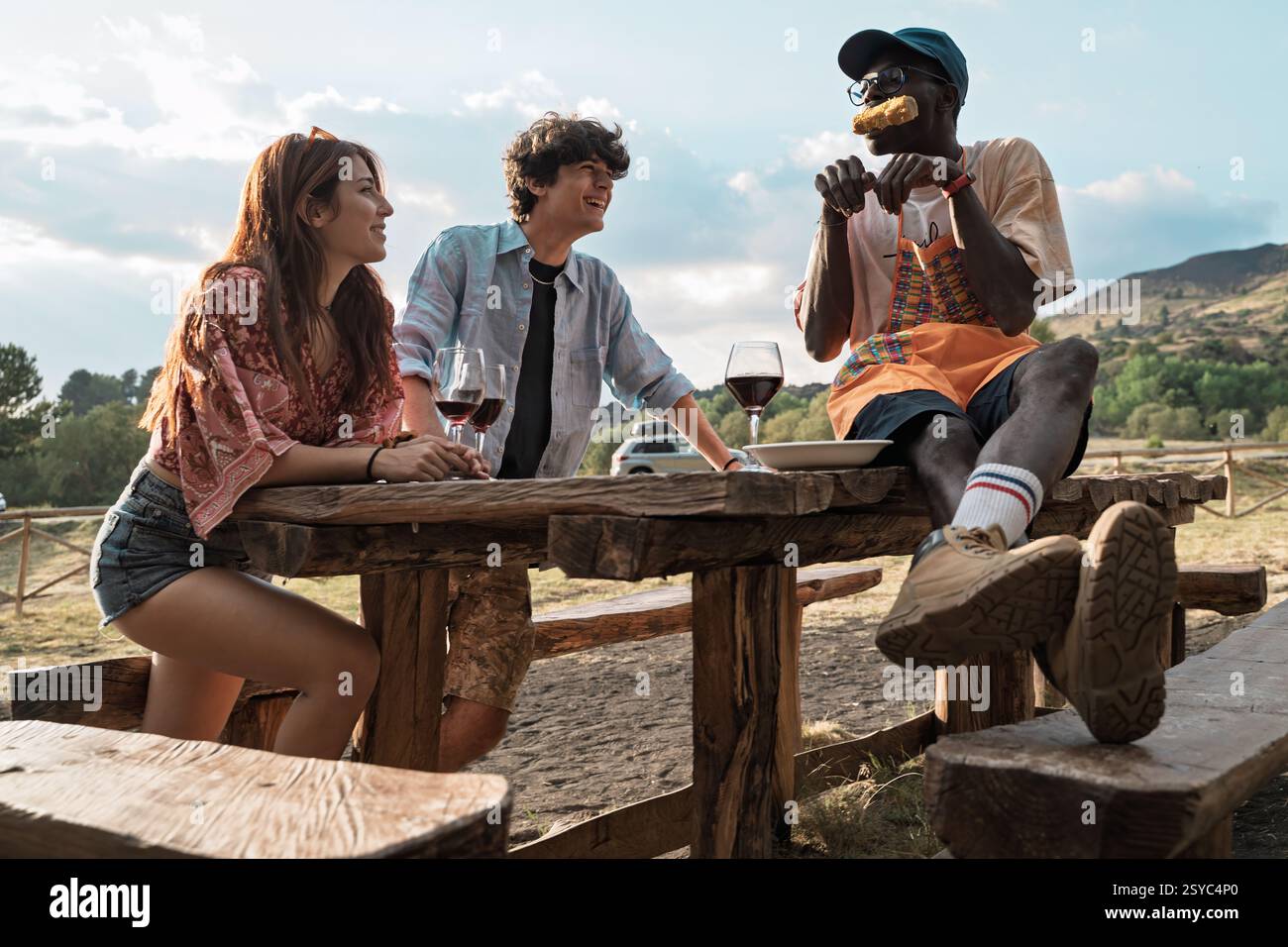 A diverse group of young friends enjoying an outdoor dinner in a scenic ...