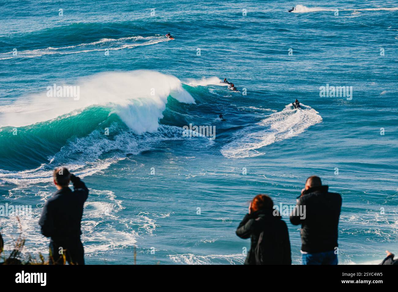 Spectators watching surfers ride massive waves in Nazaré Stock Photo ...