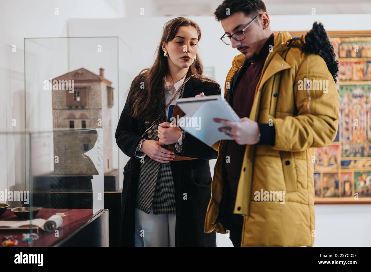 Two individuals exploring a historical exhibit and taking notes in a ...