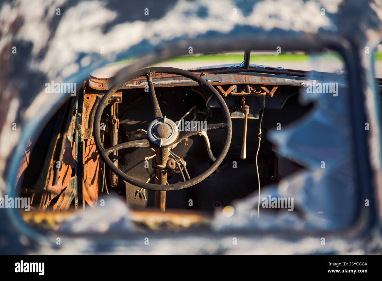 Car's steering wheel is missing. The car is old and rusted. The window ...