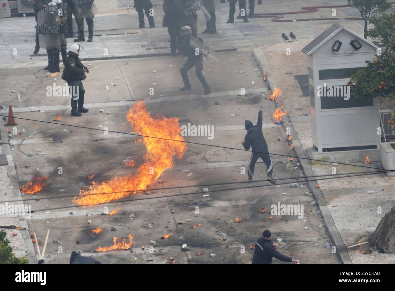 A hooded protester throws a stone against riot police at the Greek ...