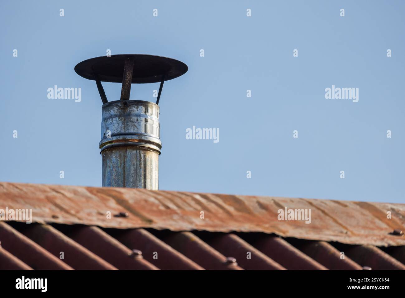 Metal chimney pipe with a protective cover on a corrugated roof. The ...
