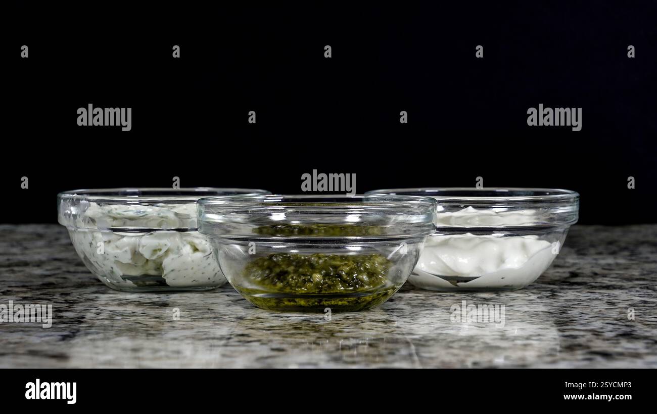 Three glass bowls filled with different sauces are displayed on a ...