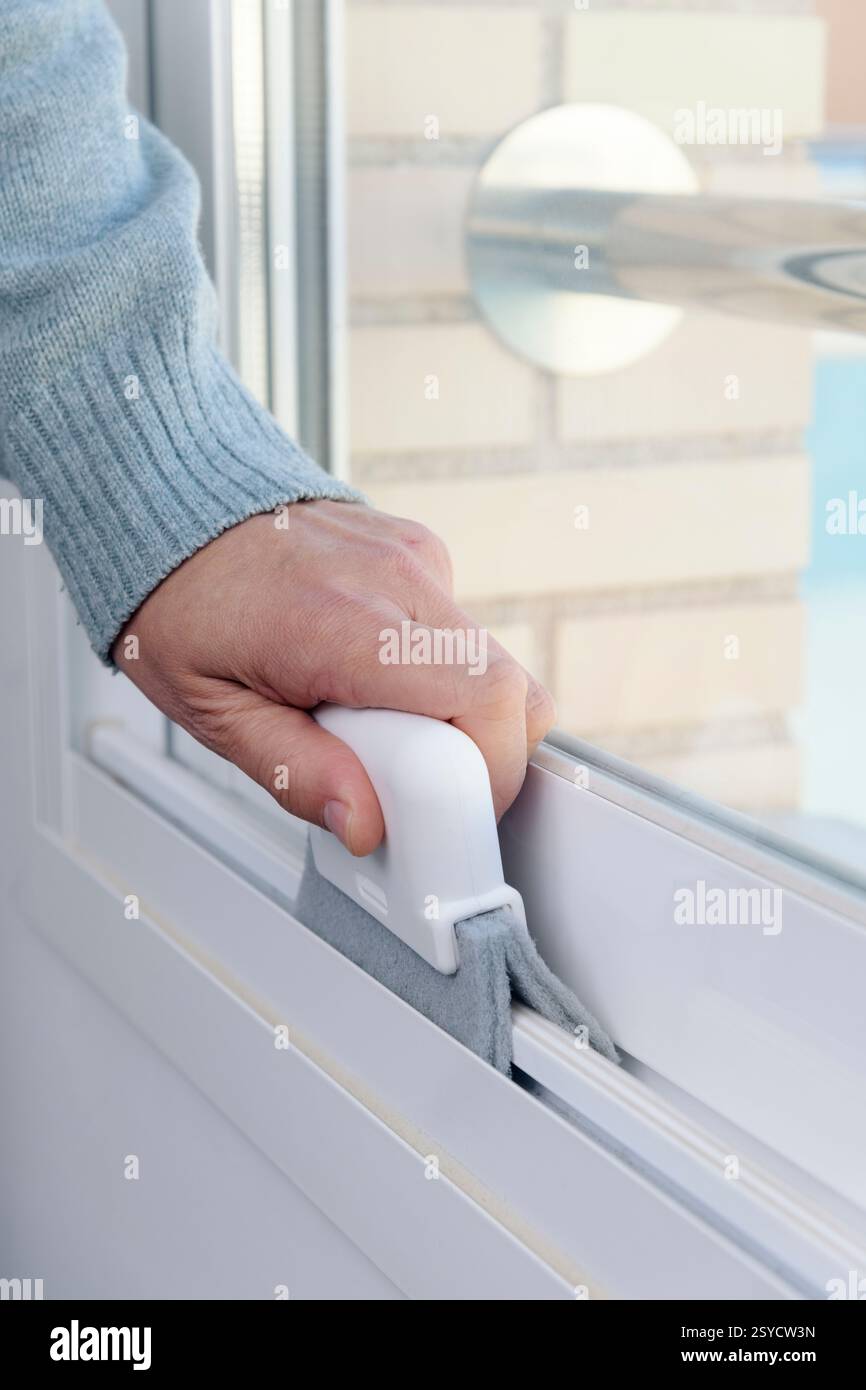man cleaning the grooves of a white aluminum sliding window frame using ...