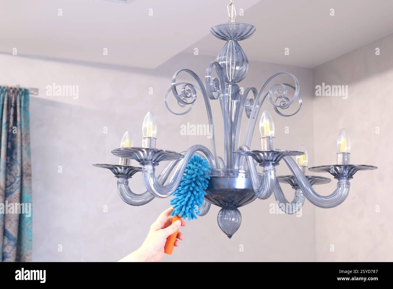 Woman wipe dust on glass chandelier with fluffy broom in living room ...