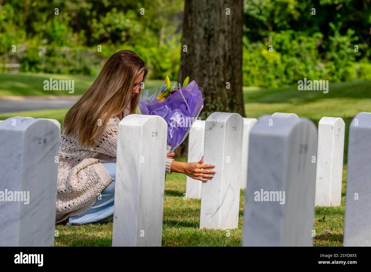 A young bride kneels at a military cemetery amid uniform rows of graves ...