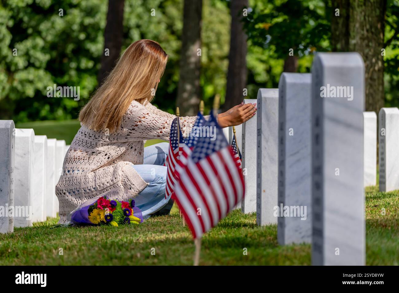 A young bride kneels at a military cemetery amid uniform rows of graves ...