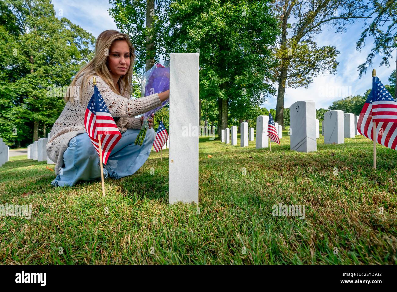 A young bride kneels at a military cemetery amid uniform rows of graves ...