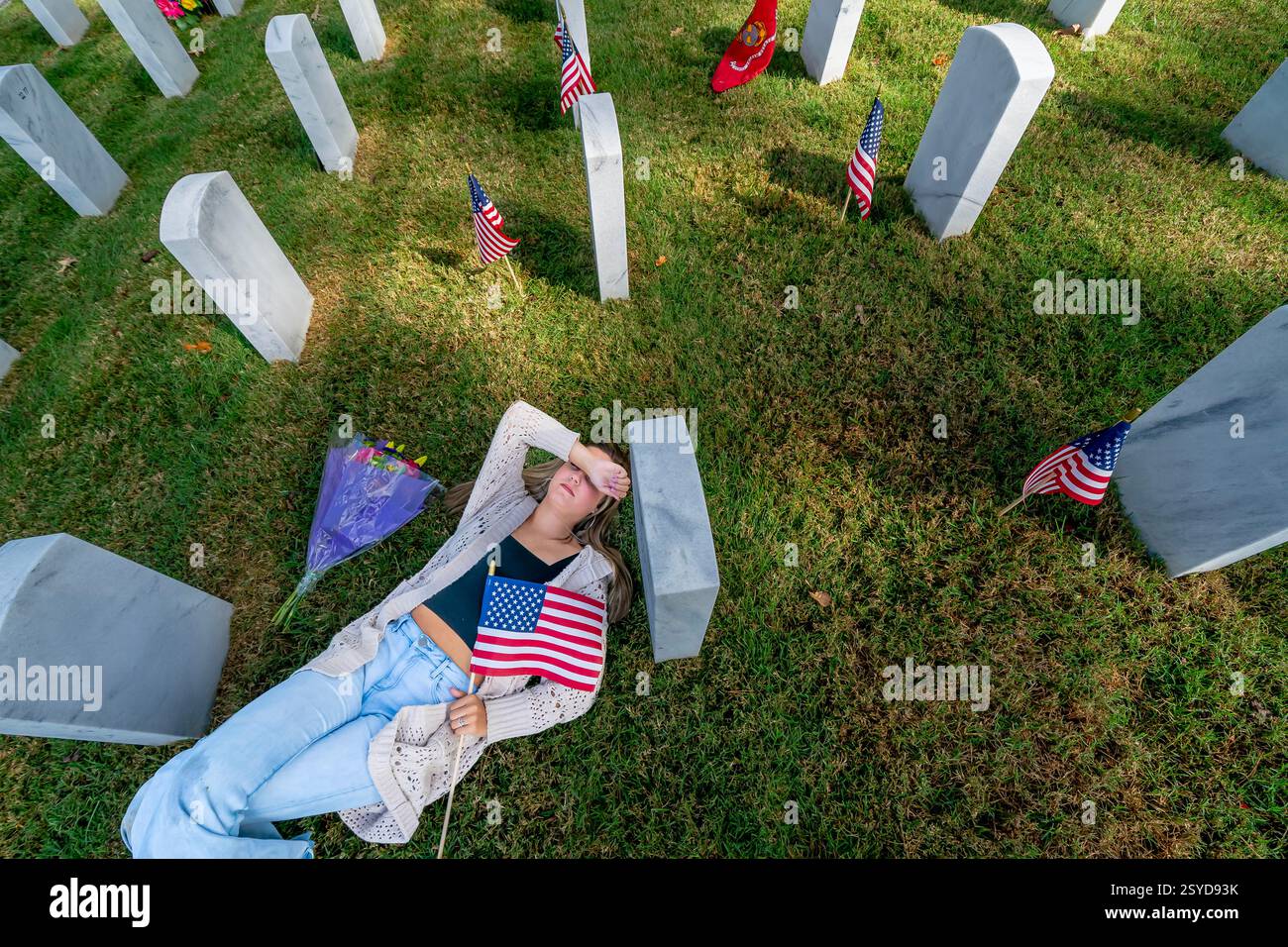 A young bride kneels at a military cemetery amid uniform rows of graves ...