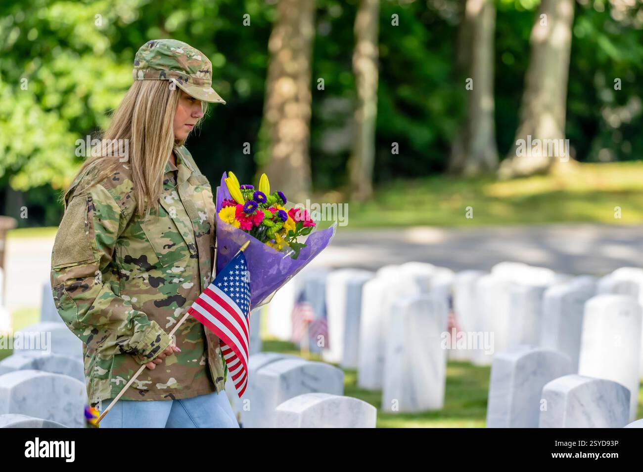 A young bride kneels at a military cemetery amid uniform rows of graves ...