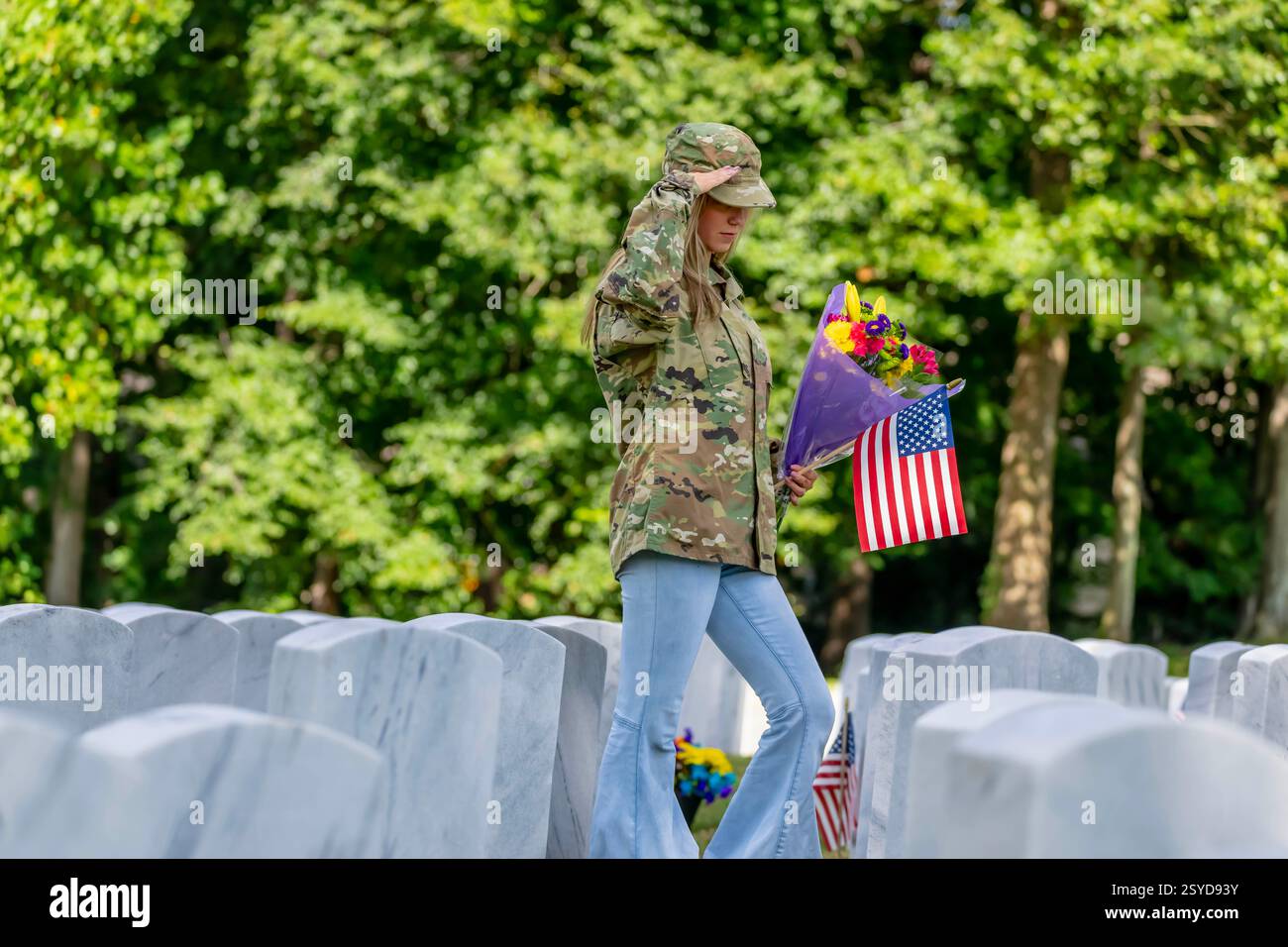 A young bride kneels at a military cemetery amid uniform rows of graves ...