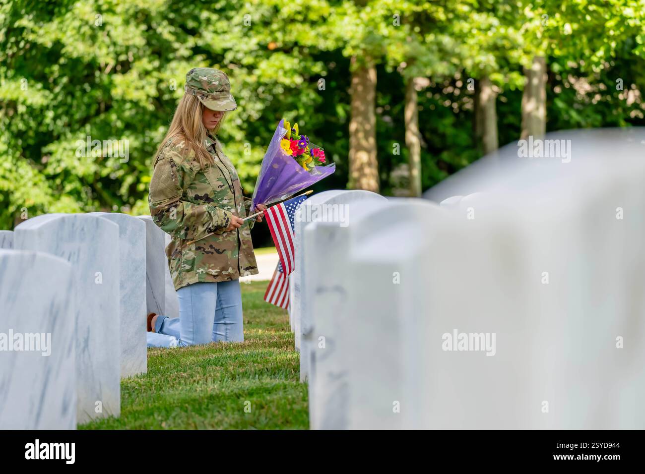 A young bride kneels at a military cemetery amid uniform rows of graves ...