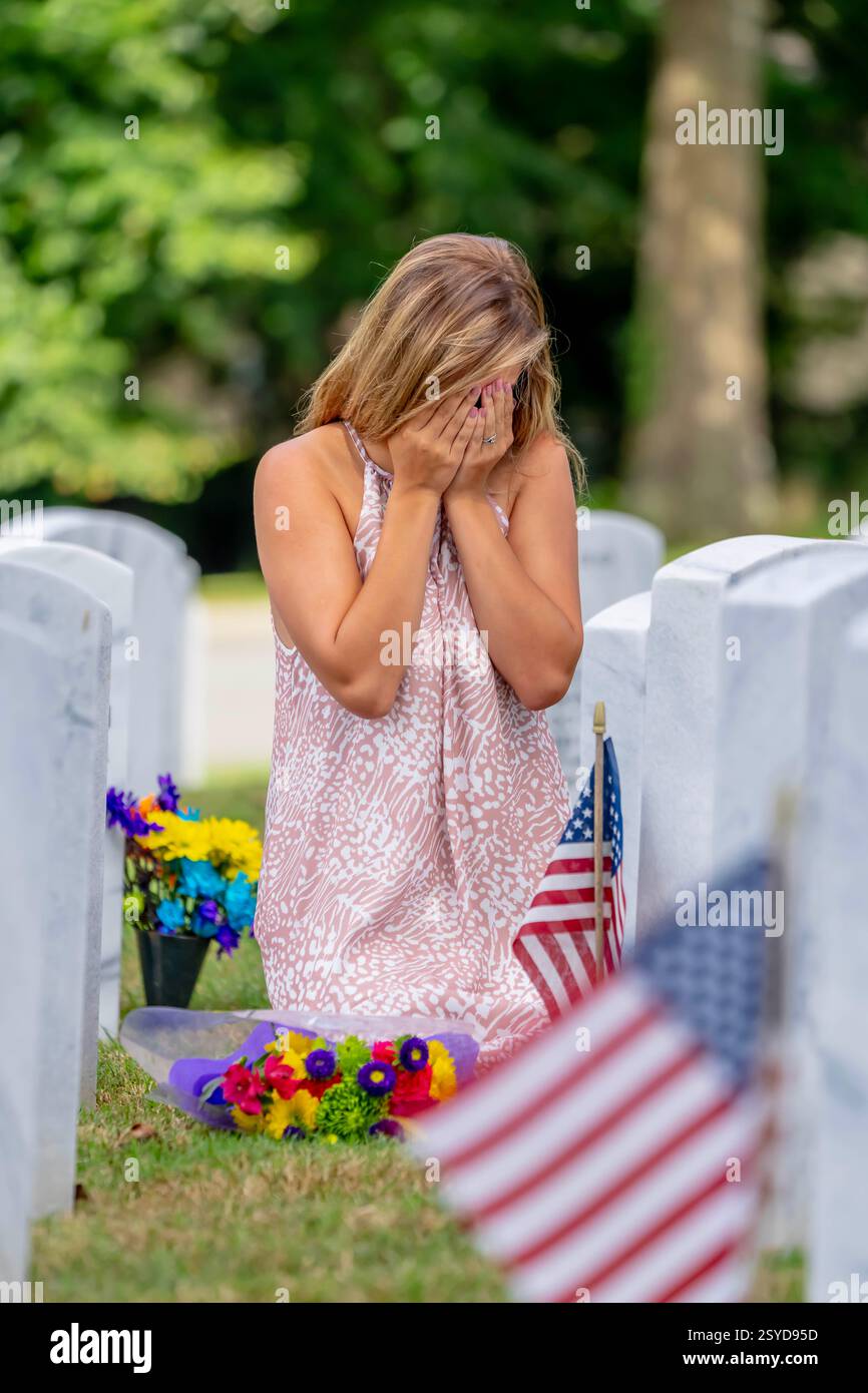 A young bride kneels at a military cemetery amid uniform rows of graves ...