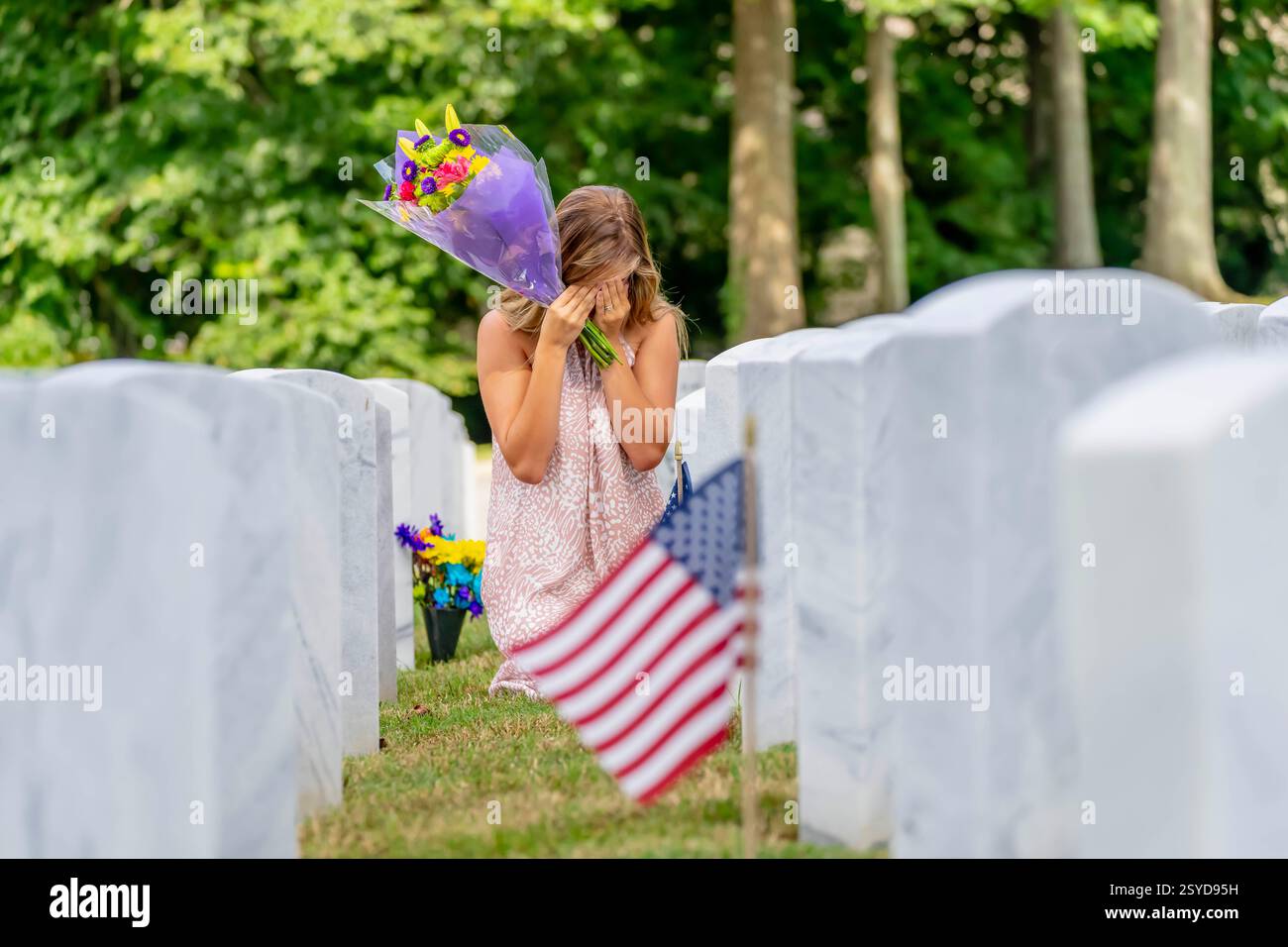 A young bride kneels at a military cemetery amid uniform rows of graves ...