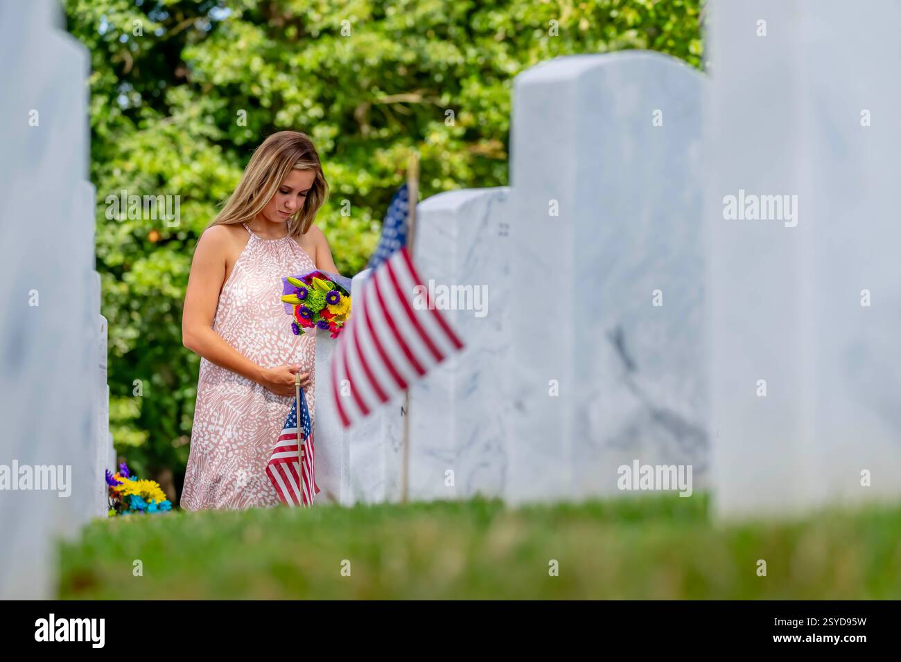 A young bride kneels at a military cemetery amid uniform rows of graves ...