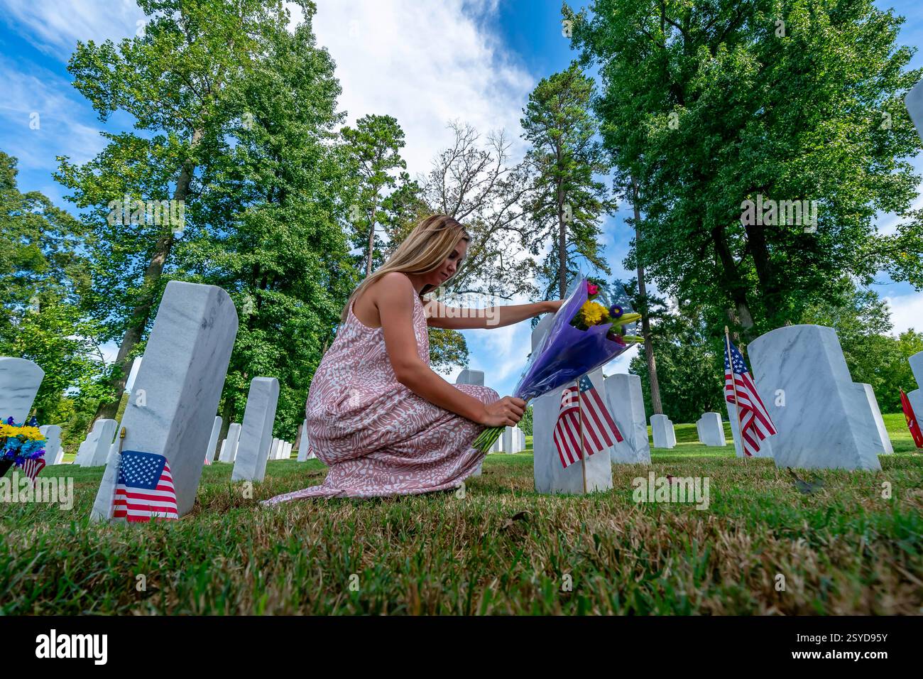 A young bride kneels at a military cemetery amid uniform rows of graves ...