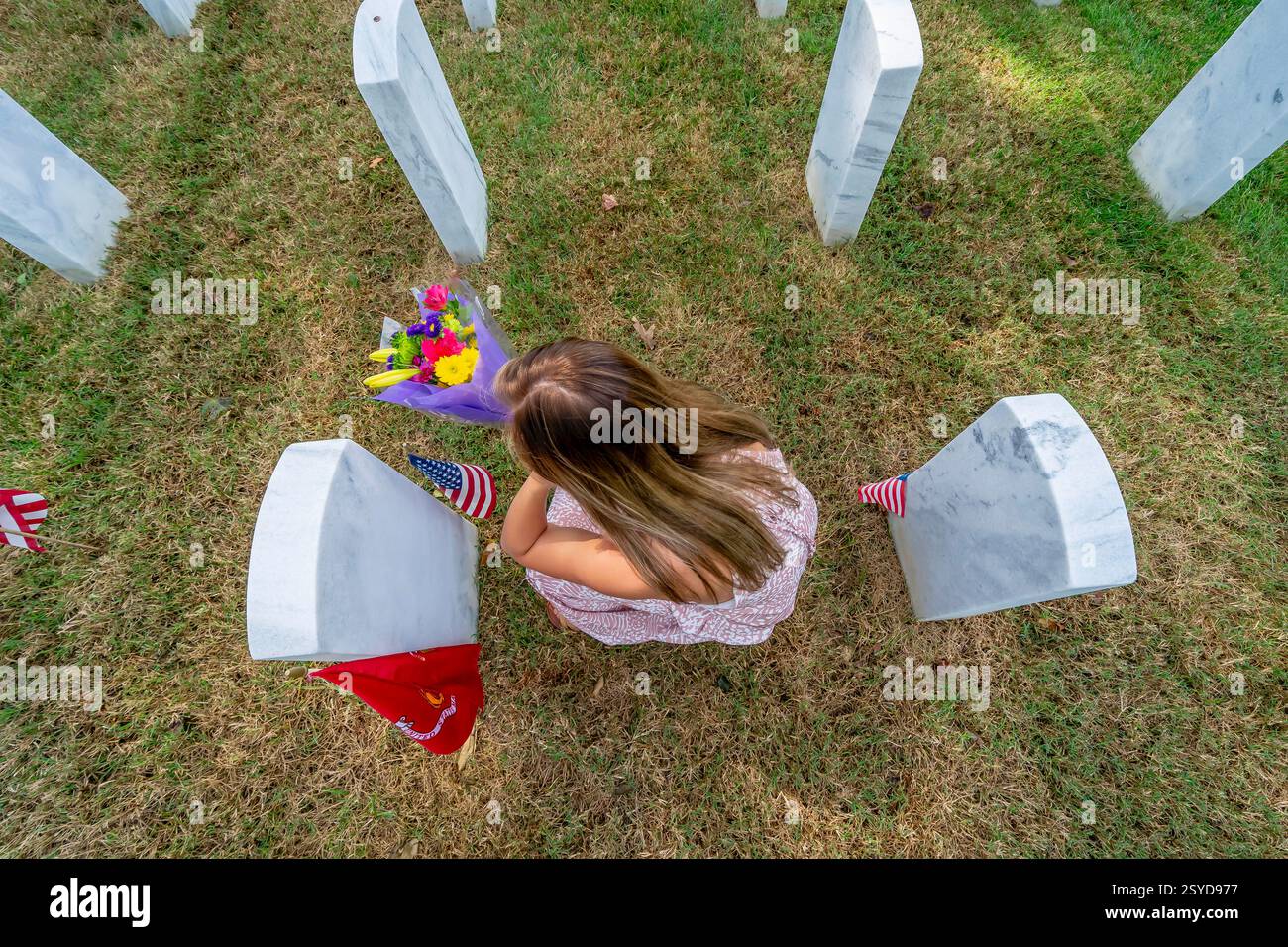 A young bride kneels at a military cemetery amid uniform rows of graves ...