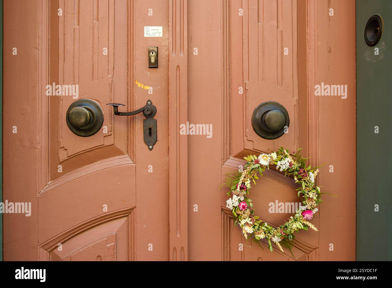Detail of an antiquated front door with floral wreath and advertising ...