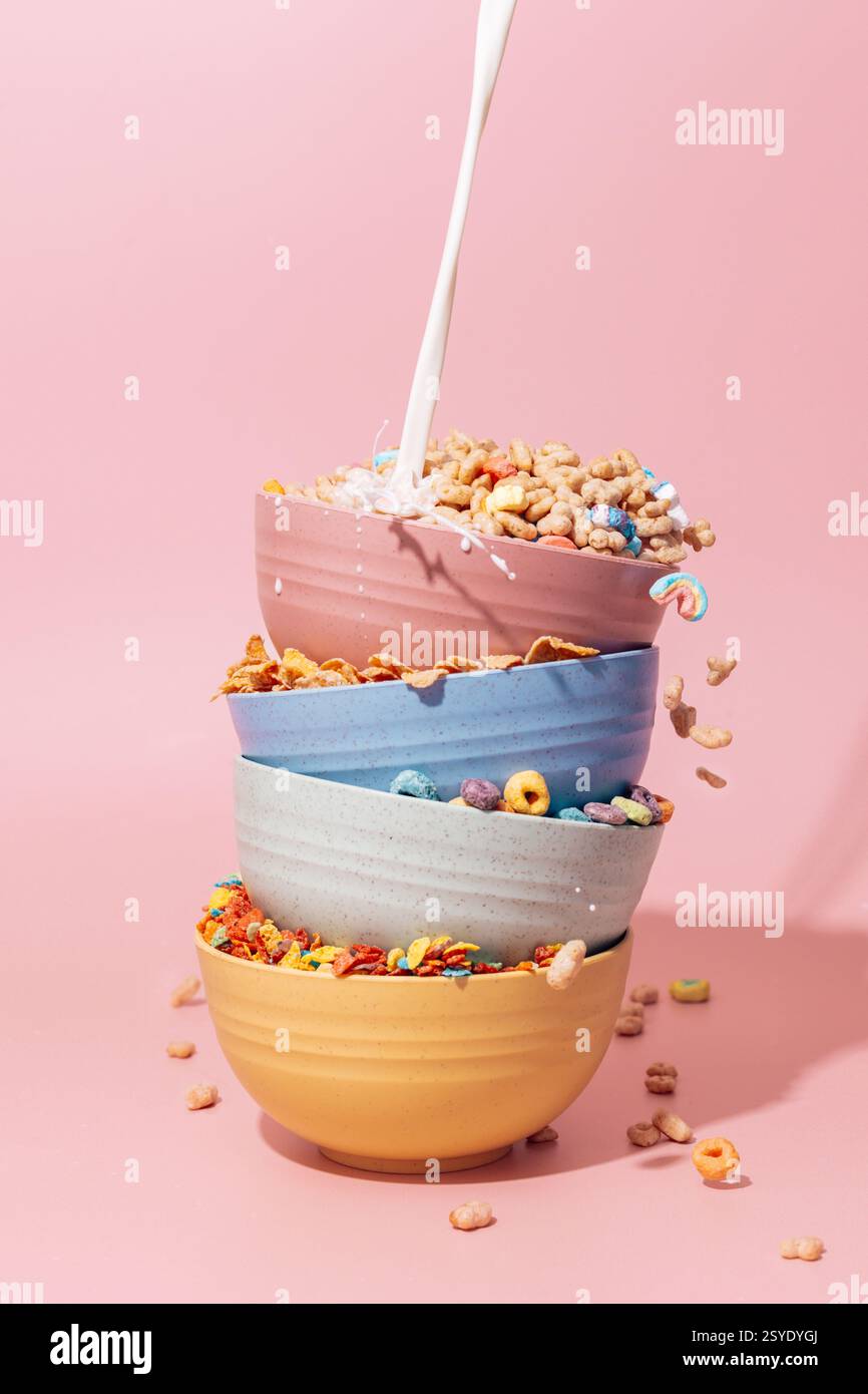 A stack of colorful cereal bowls overflows with cereal as milk pours in ...