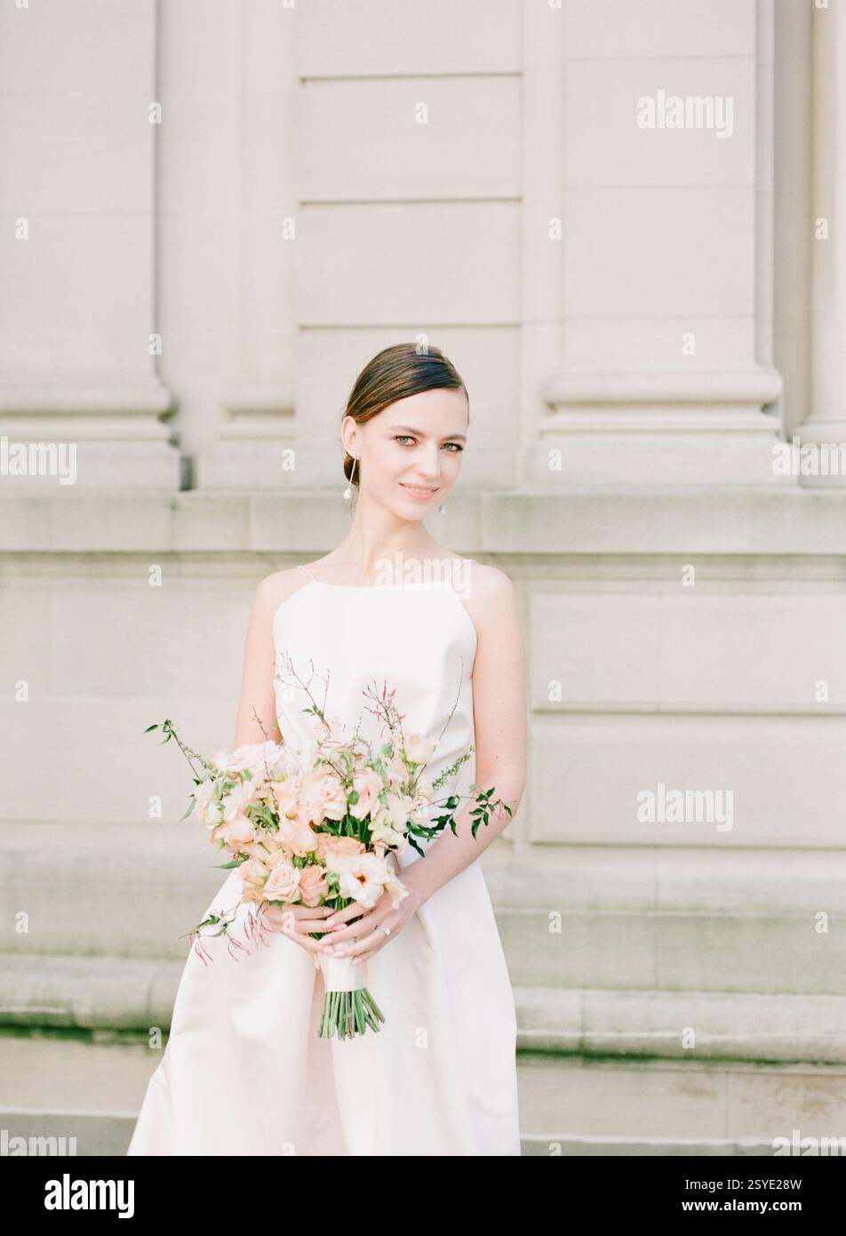 A bride stands gracefully outside a historic building, holding a ...