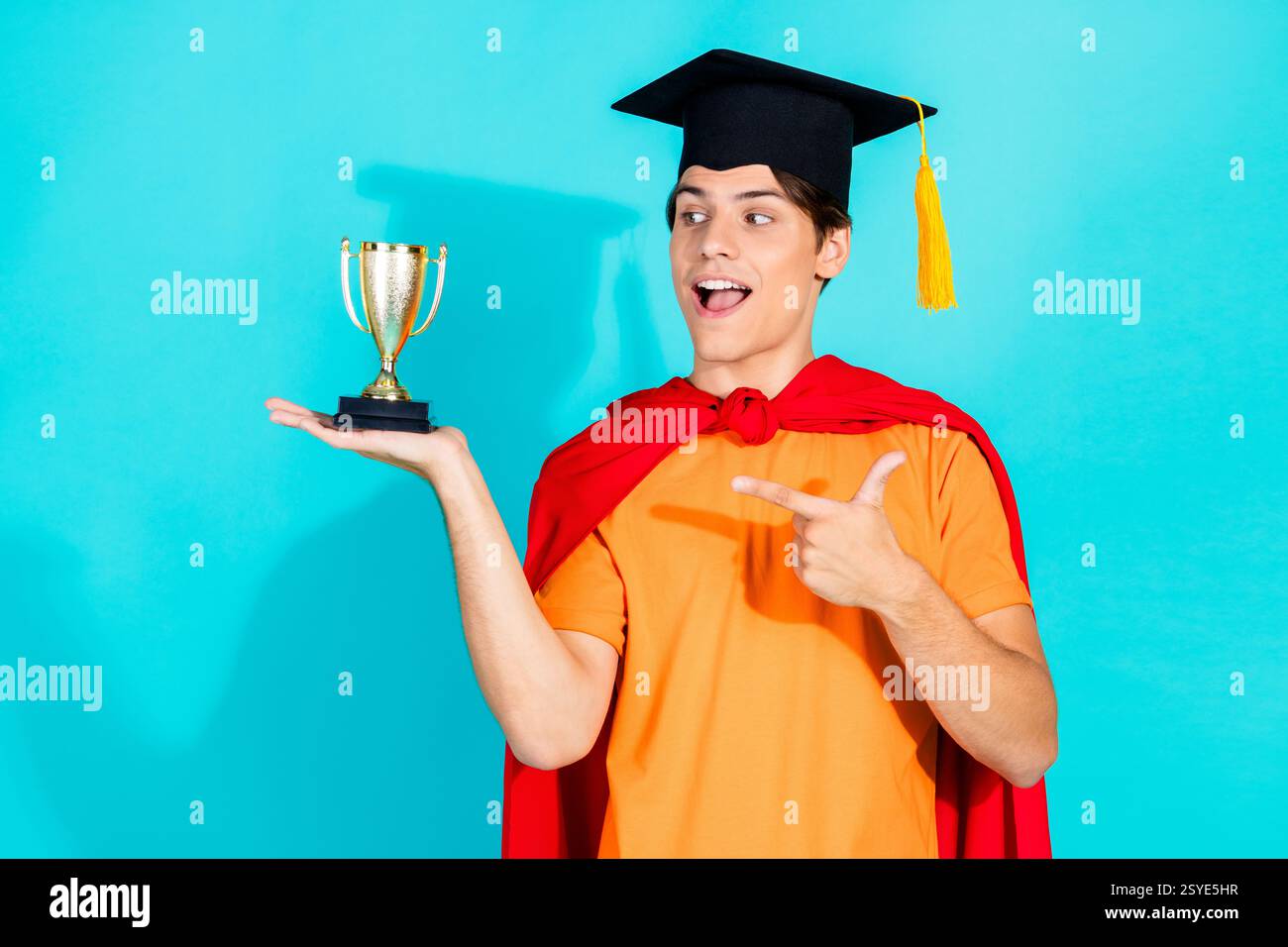 Young man with graduation cap holding trophy on teal background ...