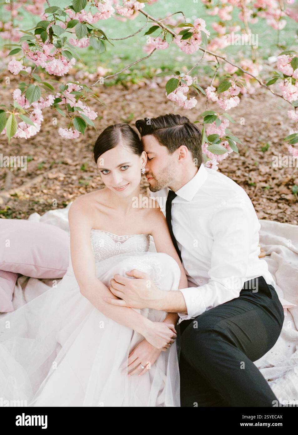 A bride and groom share an intimate moment on a blanket surrounded by ...