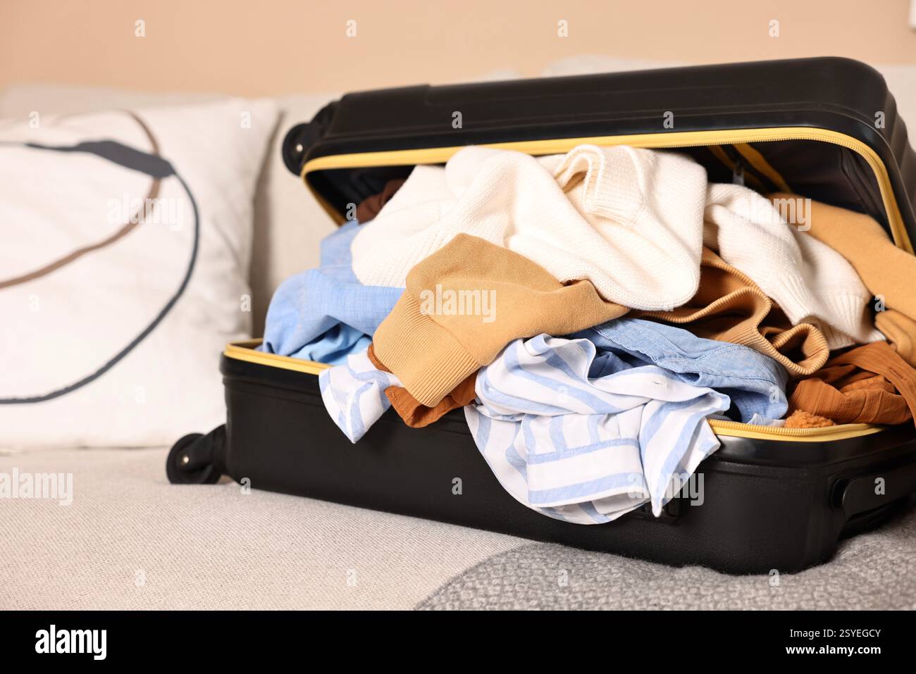 Open suitcase full of different messy clothes on sofa indoors Stock ...