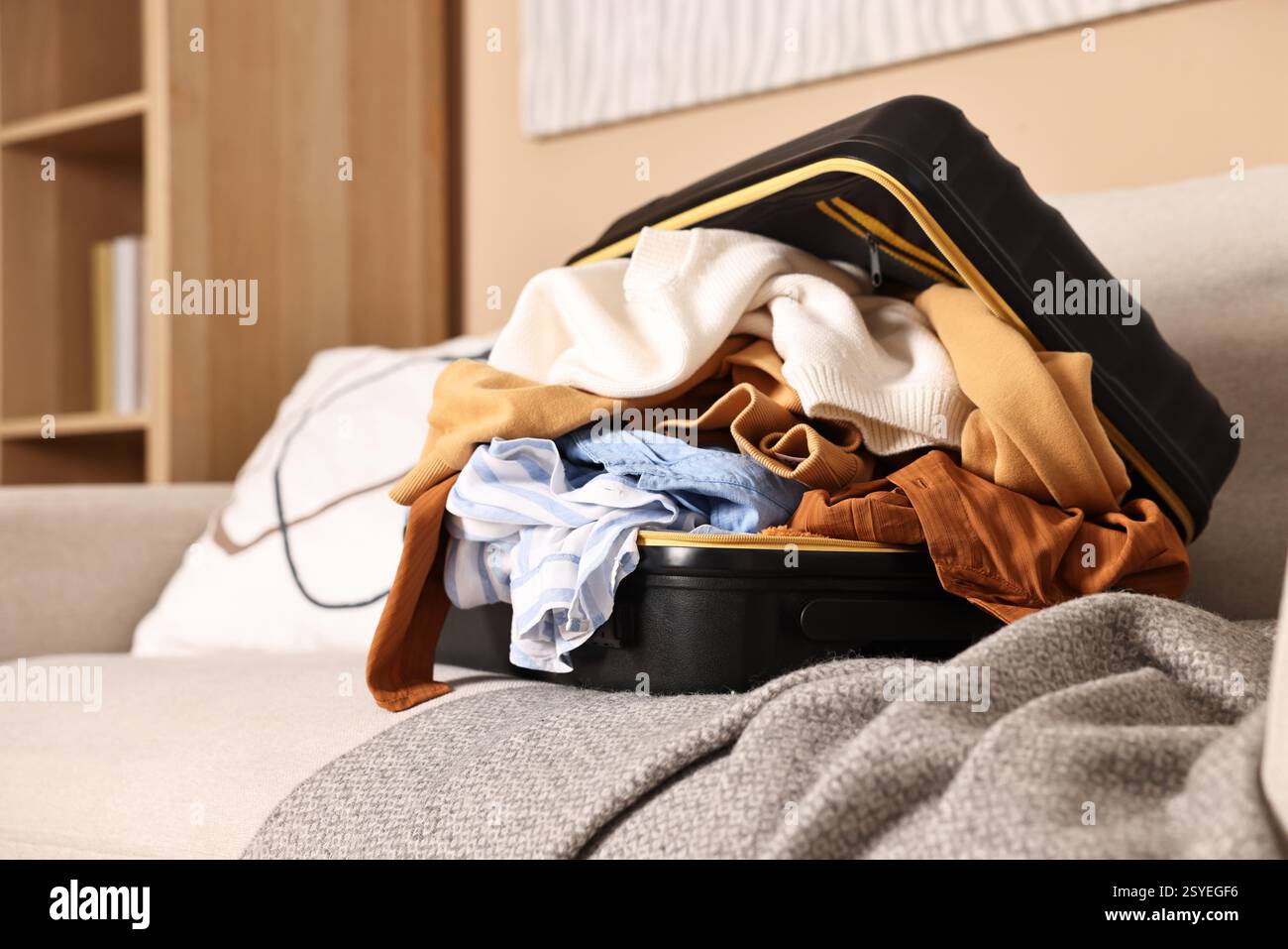 Open suitcase full of different messy clothes on sofa indoors Stock ...