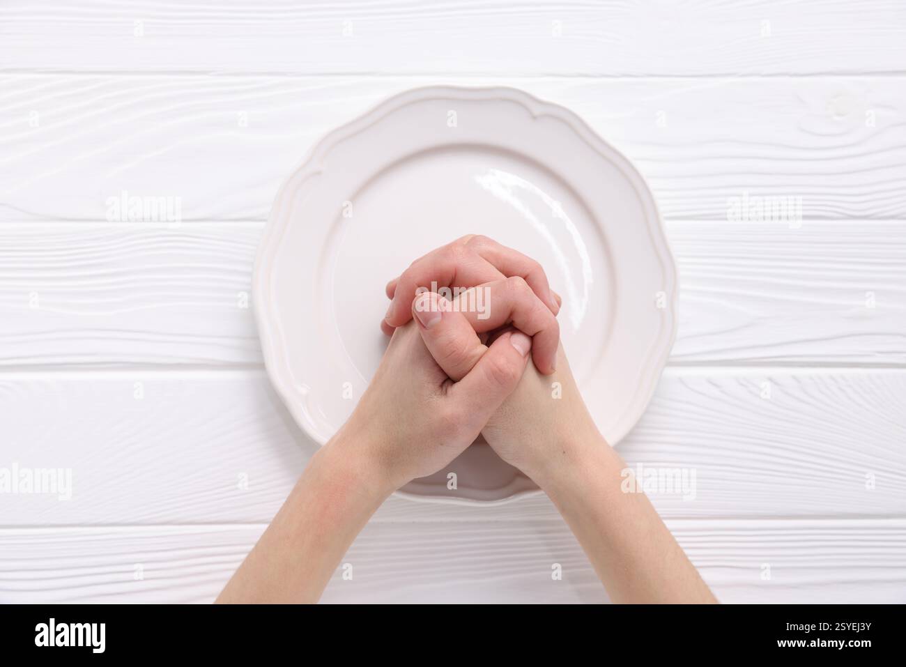 Woman holding hands together over plate at white wooden table, top view ...