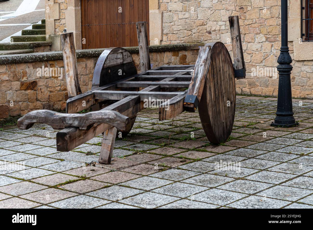 A traditional wooden cart with large wheels, placed on a cobbled street ...