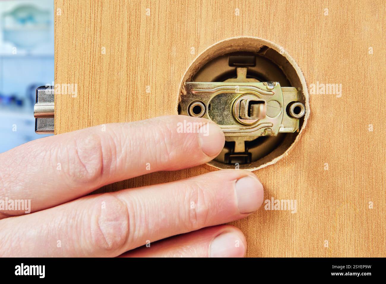 Brass latch hardware is positioned inside pre-cut hole in wooden door ...