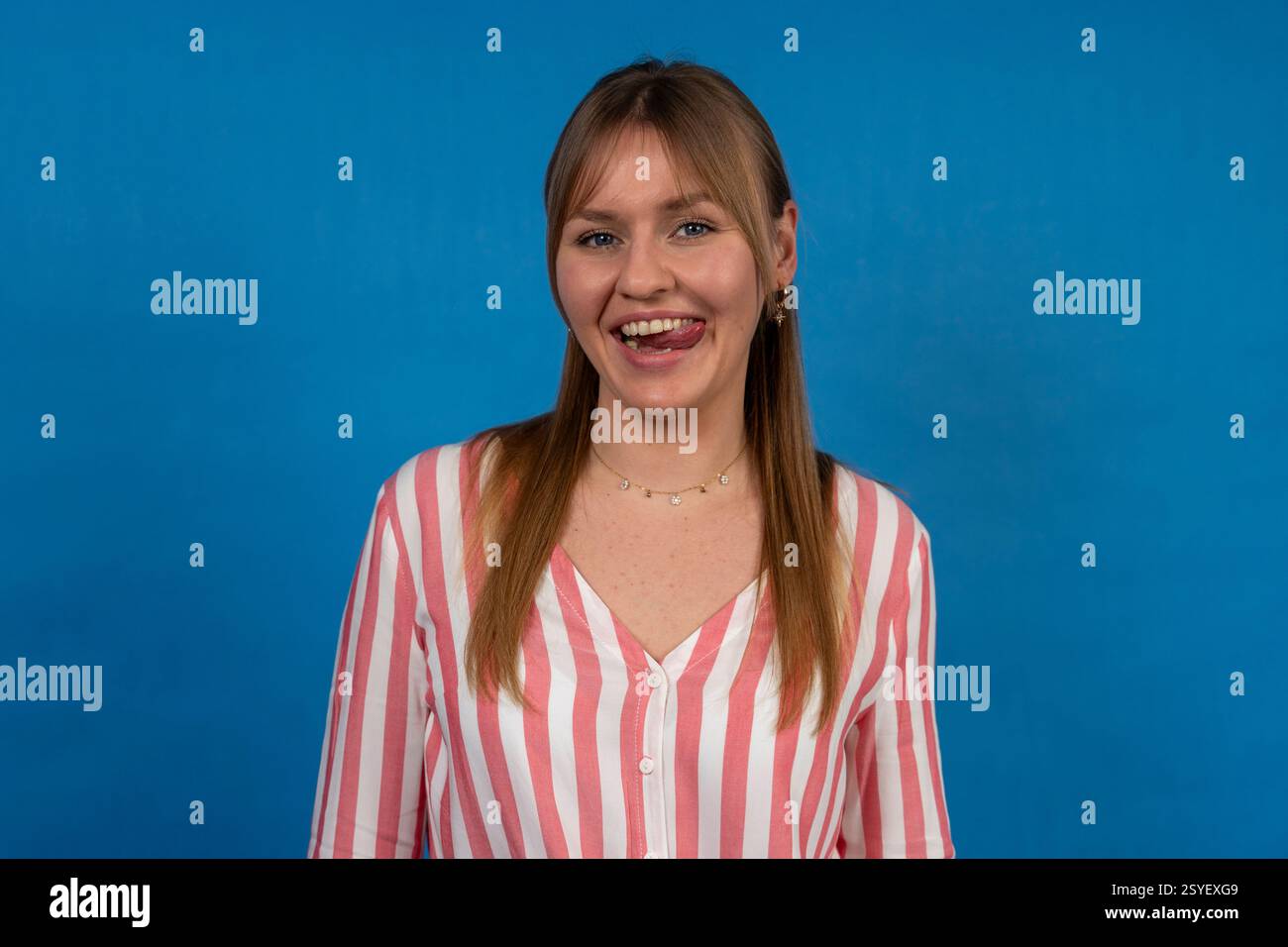 Playful young woman sticking out her tongue in a studio shot with blue background Stock Photo ...