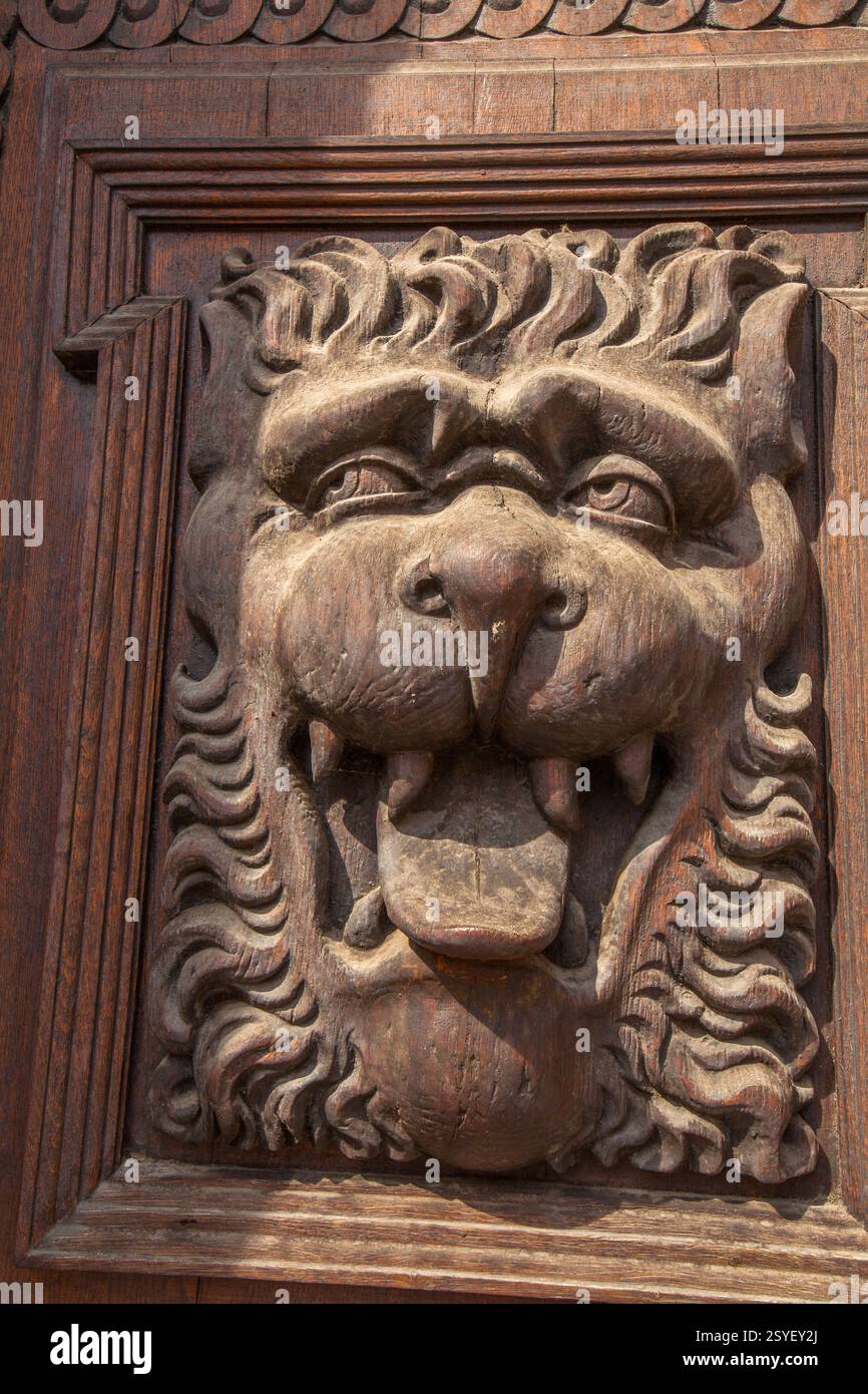 Close-up shot of a weathered, carved wooden panel featuring a grotesque ...