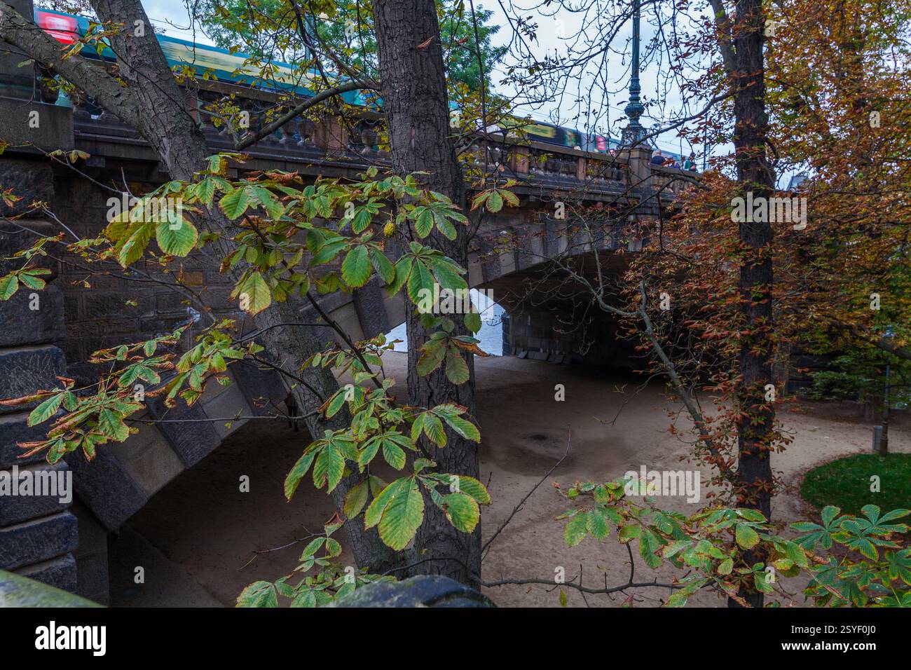 A stone bridge with ornate details spans a pathway in a park, framed by ...