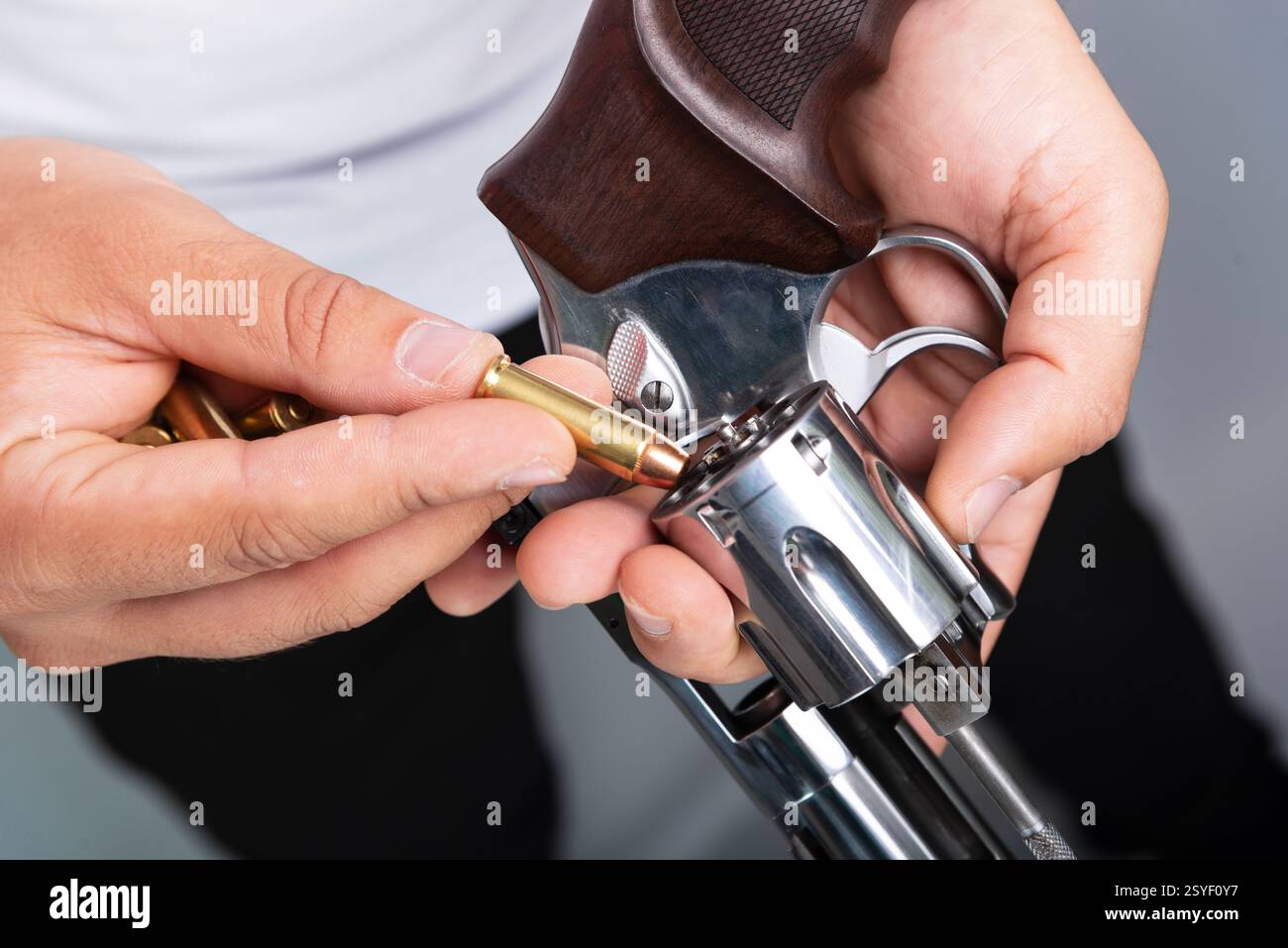 Detail of a shooting instructor loading a bullet into a silver revolver ...