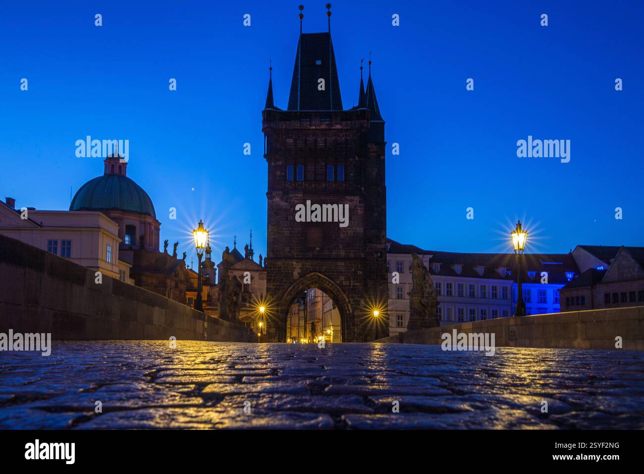 A cobblestone bridge at night leading towards a tall, silhouetted tower ...