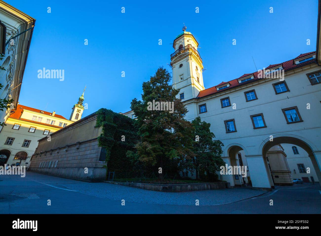 A courtyard with historic buildings, featuring a tall tower with a ...