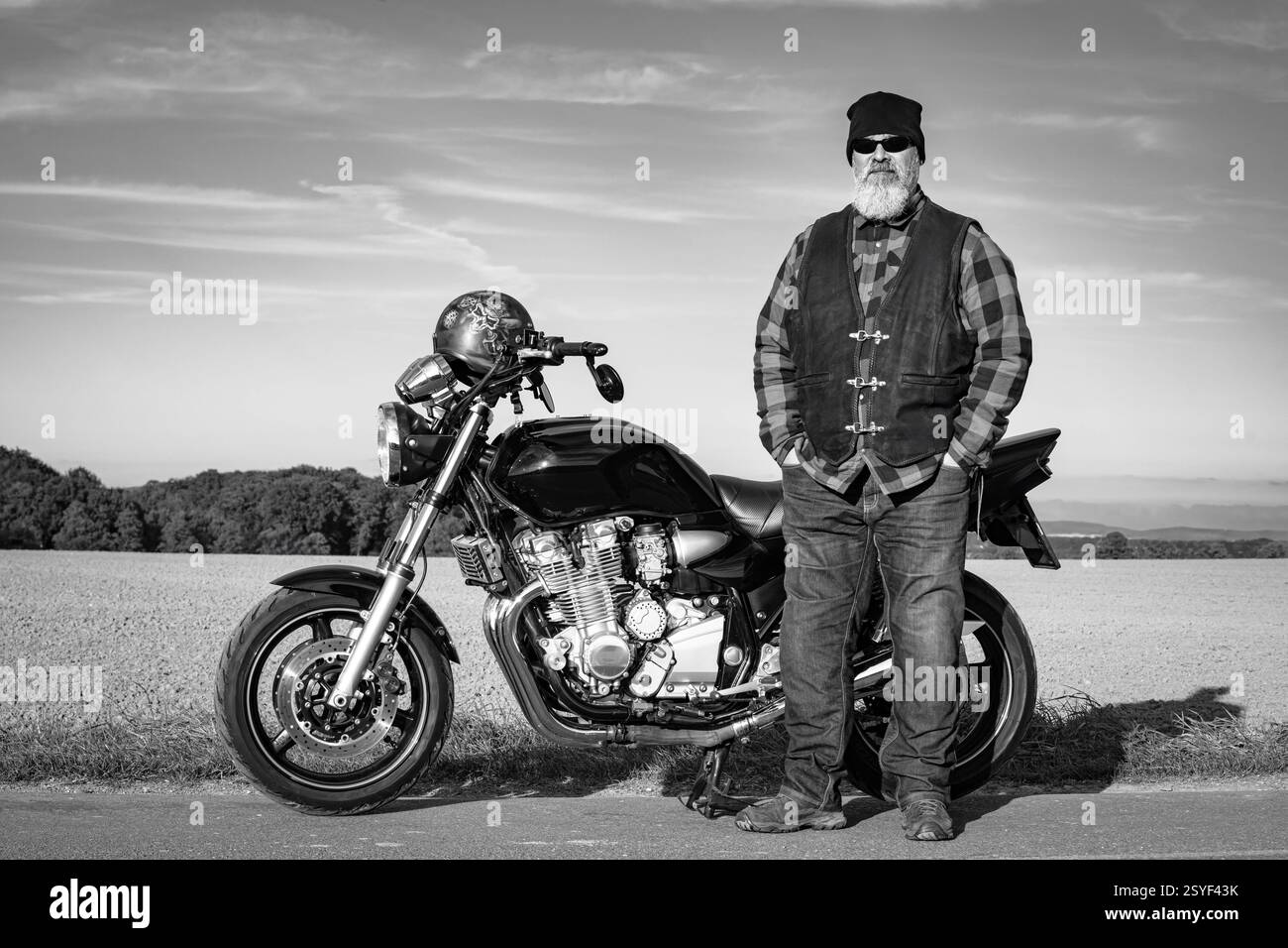 Cooler Biker steht auf einer Landstrasse vor seinem Motorrad., Aufnahme ...