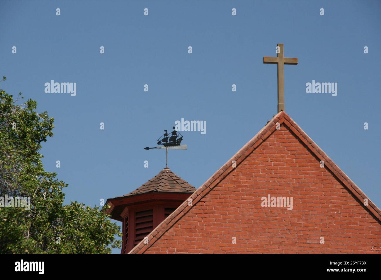 A cross on top of a church building and a sailing ship weather vane on ...