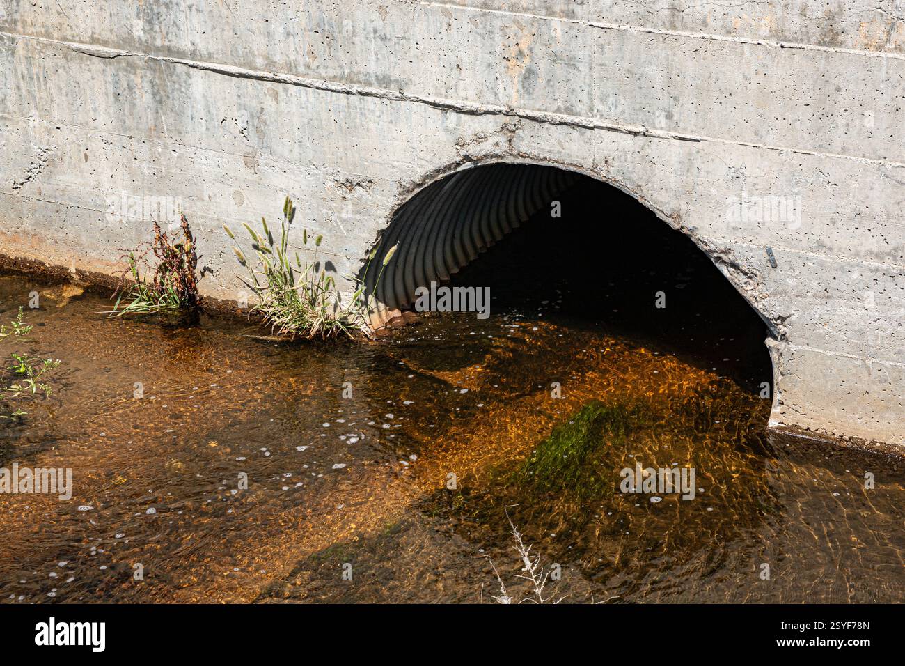 A corrugated metal culvert allows water to flow under a concrete ...