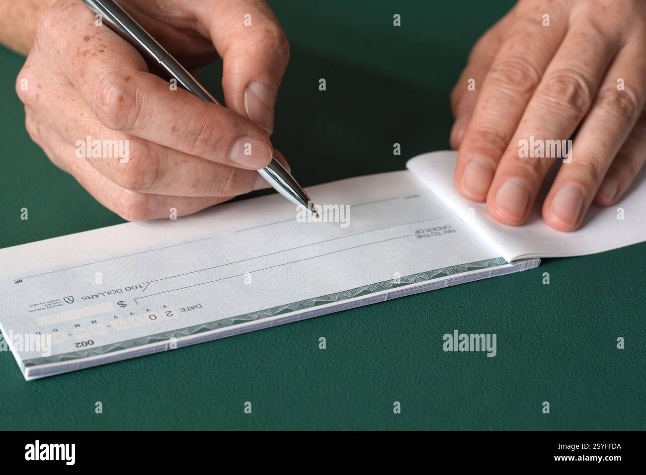 Closeup woman's hands writing bank cheque on green background Stock ...