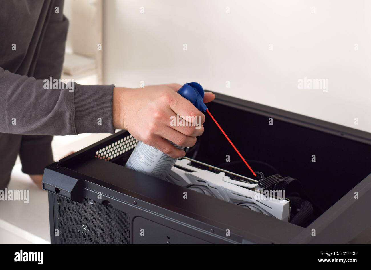 Young man cleaning the inside of a computer with compressed air duster ...