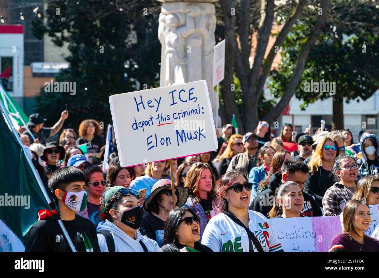 A participant in the crowd holds up a sign asking ICE to deport Elon ...
